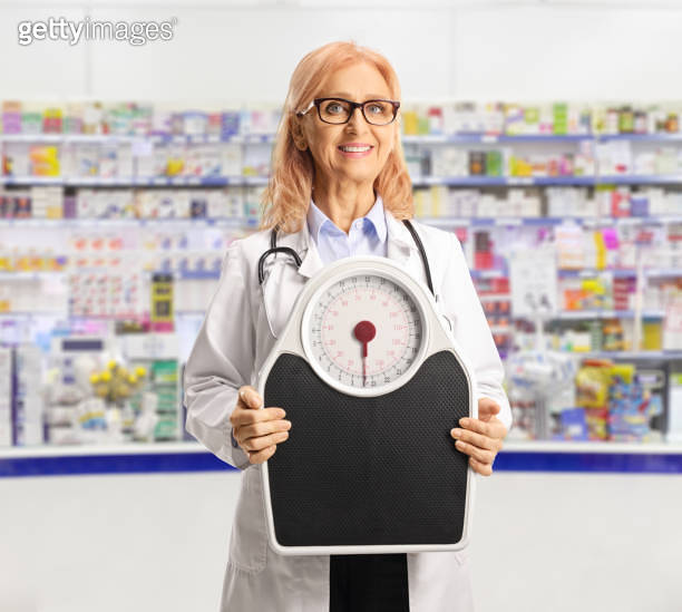 Smiling female doctor holding a weight scale in a pharmacy (1453873020 ...