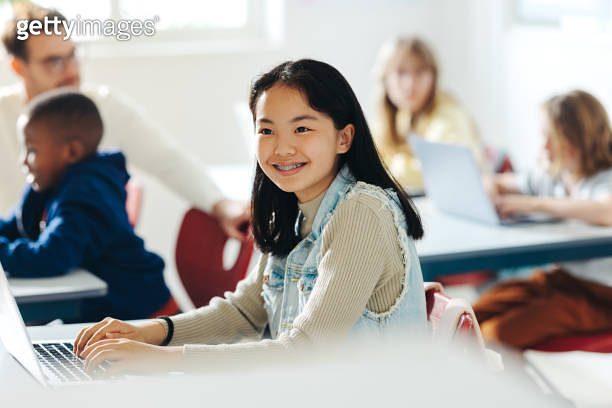 Happy Asian girl enjoying a coding class, using a laptop to engage in ...