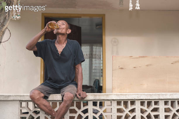 A poor middle aged drinks a cold bottle of light beer while sitting on ...