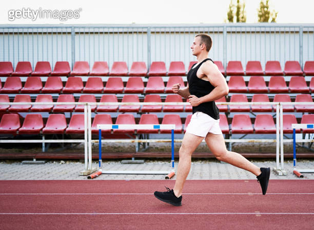 Young muscular fit male sprinter running on a red running track ...