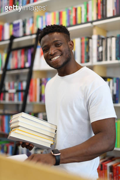 A cheerful young student in a university library, surrounded by books ...
