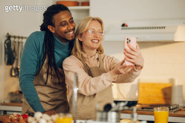 A happy multicultural couple is taking self-portraits in the kitchen ...