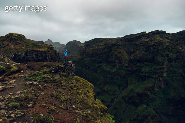 A man on a cliff is looking down into a chasm in the mountains of ...