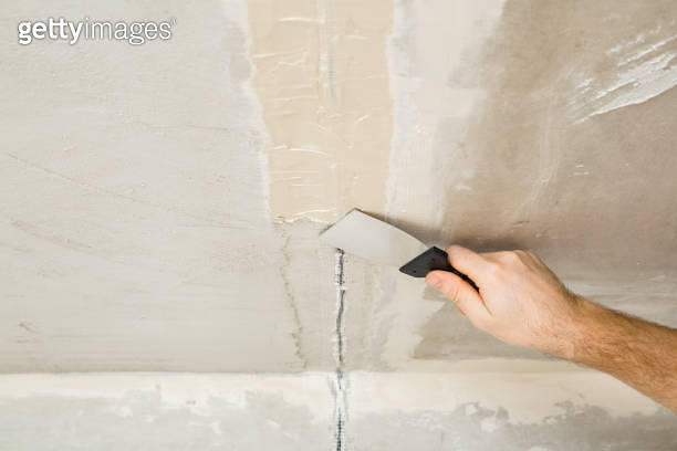 Young adult man hand using spatula and plastering concrete ceiling with ...