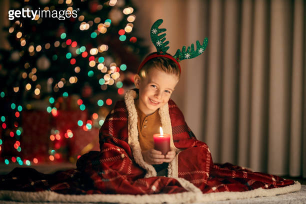 Portrait of a festive boy sitting at home with candle in hands and ...