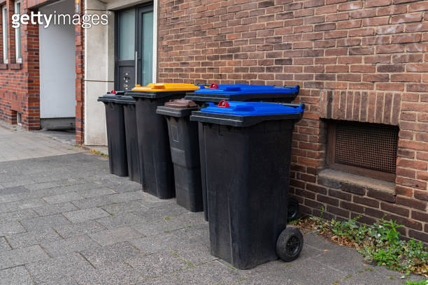Plastic trash cans with colorful lids stand near a brick wall of a ...