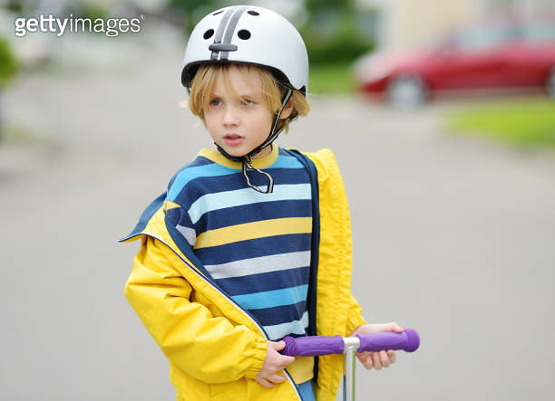 Little boy in safety helmet is riding scooter. Child is bored without ...