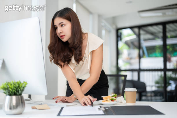 A focused Asian businesswoman is bending over a table and looking at ...
