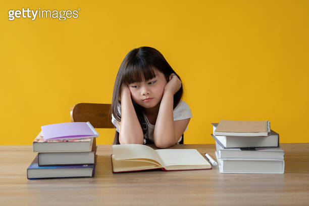 A cute young Asian girl sitting at her study table with a bored face ...