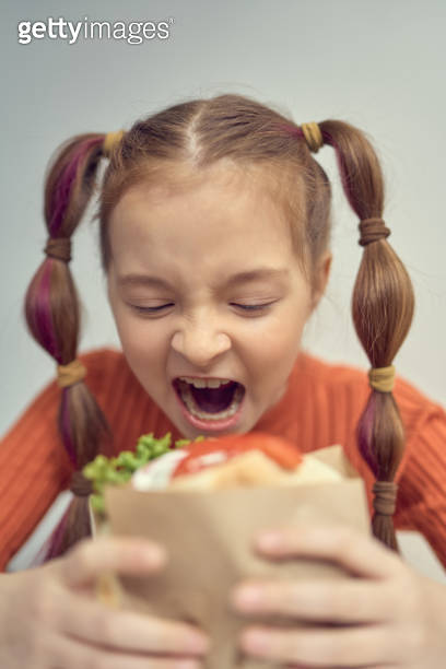 Hungry little girl biting a sandwich. Portrait of a funny white kid ...