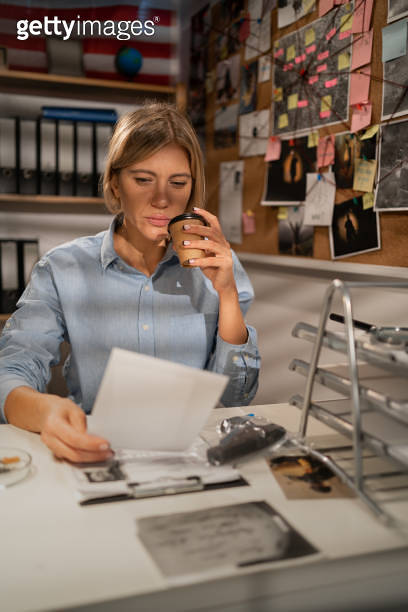 Detective drinking coffee and working at desk in her office 이미지 ...