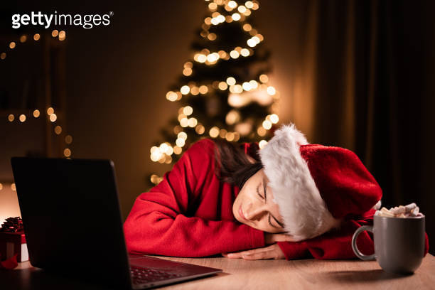 Tired young woman sleeping in front of laptop sitting in decorated room ...