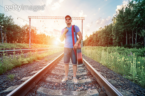Traveler man wearing sunglasses stands on rail track and holds guitar ...