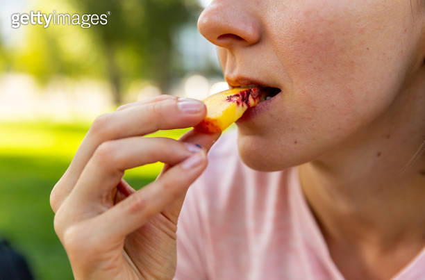Close up of mouth eating food in public. Woman holding and bites peach ...