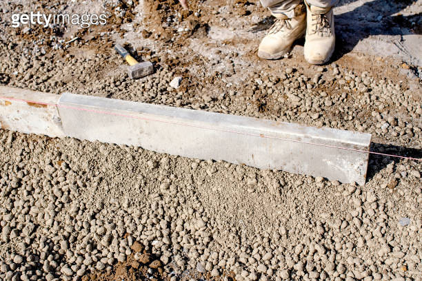 Builder placing edging pin kerb on semi-dry concrete using a string ...