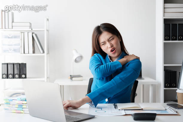 Businesswoman suffering shoulder pain sitting in a chair while working ...