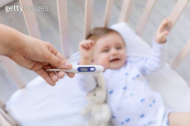 thermometer in focus in mom's hands with a high temperature of 37 ...