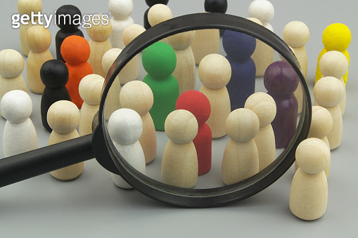 Different colored many people figures under magnifying glass on gray ...