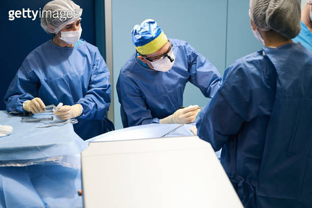 Surgeon with a head-mounted camera is leaning over operating table ...