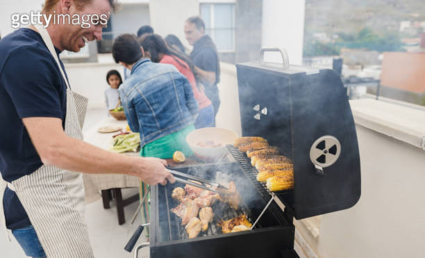 Happy friends cooking corn and chicken at barbecue rooftop dinner ...