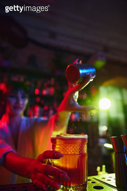 Young woman, bartender making delicious cocktail, adding powder for ...