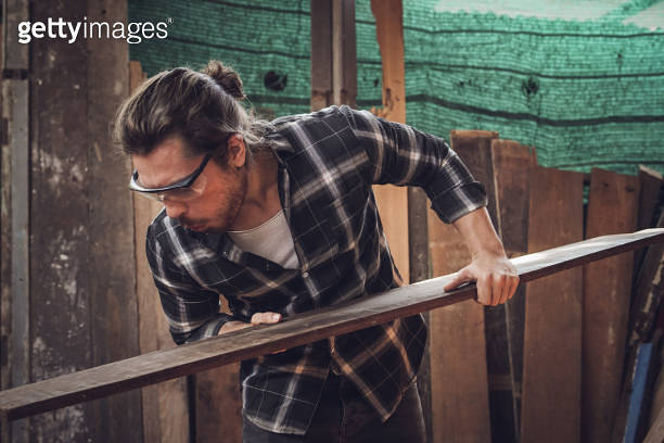 Male carpenter blowing dust on the wood board and checking quality ...