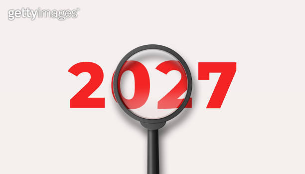 Magnifying glass magnifies the year 2027 on white background. Focusing ...