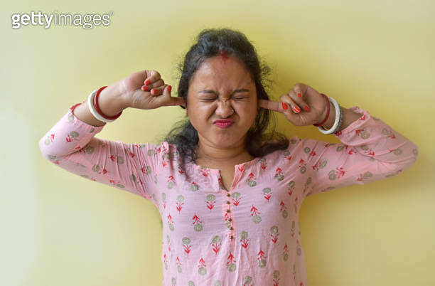 Angry annoyed young Indian woman plugging her ears to avoid loud noise ...