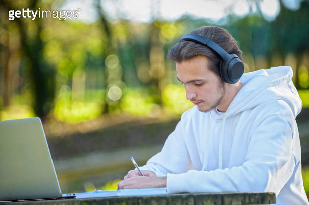 Young man writes with a pen in a notebook at a table in the park ...