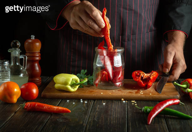 Preserving capsicum annuum in a spice jar. A cook puts red bell pepper ...