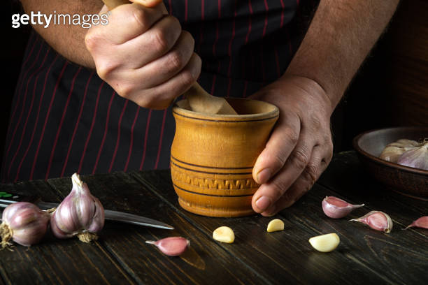 The chef crushes garlic on the kitchen table before adding it to the ...