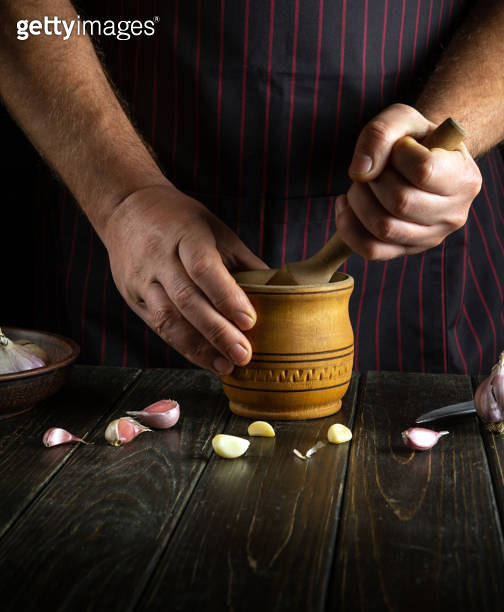 The cook crushes garlic with a wooden pestle and mortar on the kitchen ...