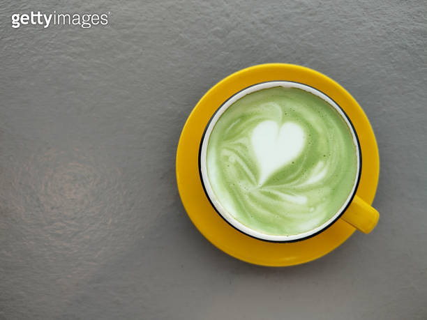 Hot green tea with heart shape latte art in yellow cup on grey ...