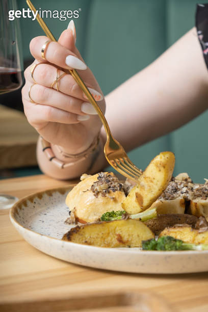 Close up of a fork in a woman's hand over a plate with delicious food ...