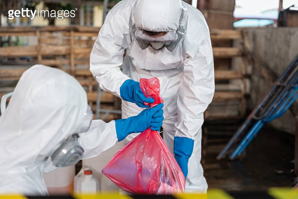 A team of two chemists, wearing PPE suits and gas masks, recover a ...