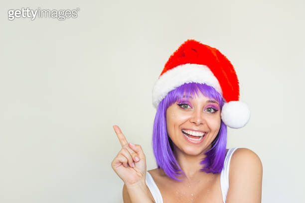 A young amazed smiling woman with violet hair in a red Santa Claus hat ...