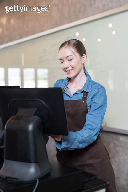 Beautiful young woman barista take order from customer in coffee shop. Female barista using ...