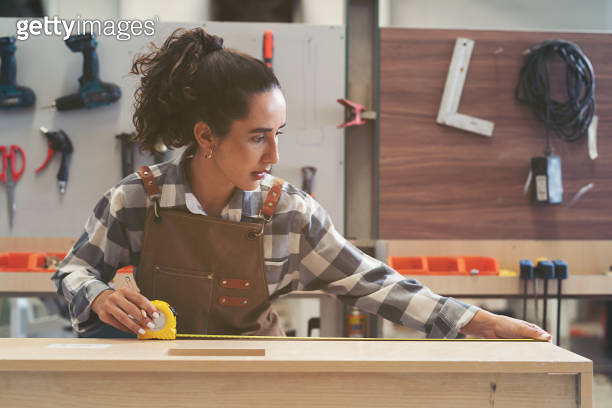 Young woman carpenter using measuring tape at carpentry workshop ...