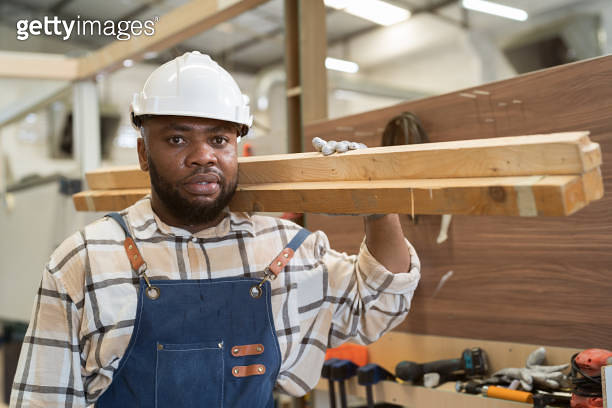 Male carpenter carrying piece of wood on his shoulder at wood ...