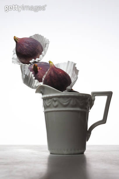 Stack of delicious fresh figs in a white ceramic cup on a white ...