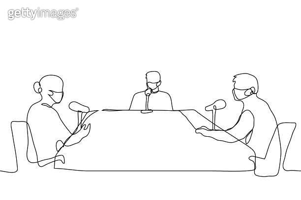 three people at a large table are sitting in masks with microphones ...