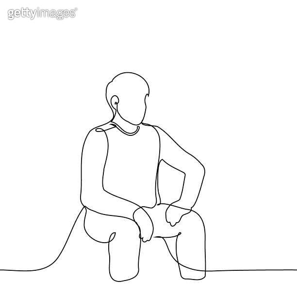 man sits in a confident pose with legs wide apart resting his palms on ...