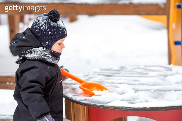 A little boy walks on the playground. A child cleans snow with a child ...