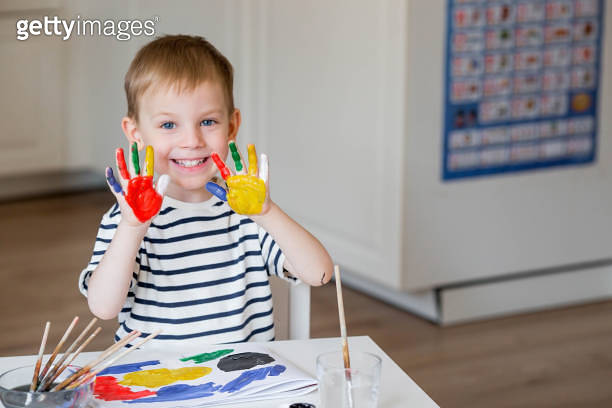 A happy little boy of 3 years old paints on paper. The child's hands ...