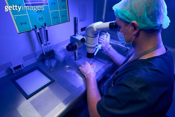 Laborant in sterile gloves and protective face mask looking at ...