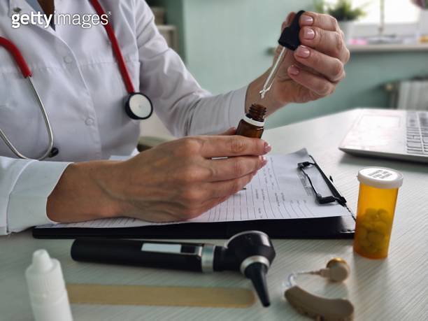 ENT doctor with otoscope holds ear drops and writes out medical ...