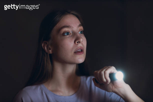 Woman scared holding hand flashlight in darkness and afraid of violence ...