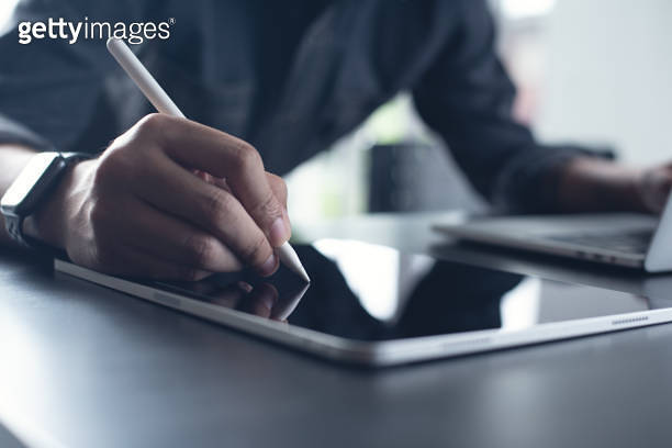 Business man, graphic designer using stylus pen on digital tablet screen while working on laptop ...