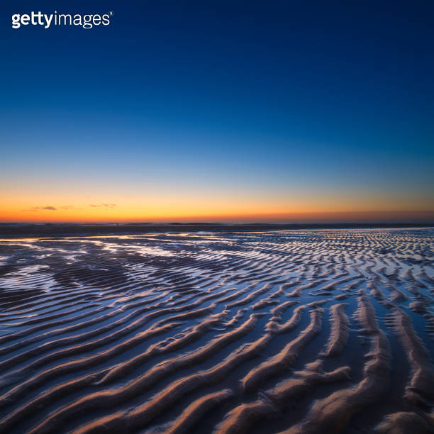 A seascape during sunset. Lines of sand on the seashore. Bright sky ...