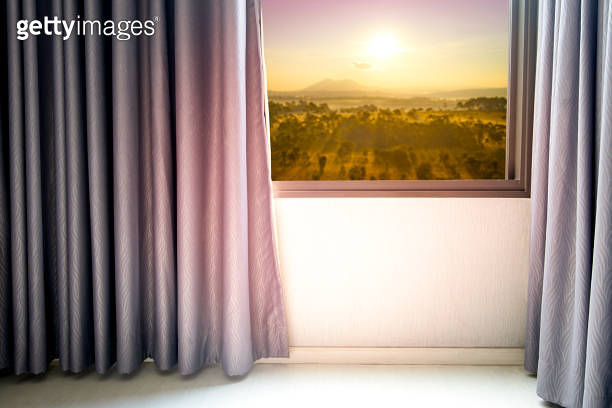 The living room is decorated with curtains and large open windows with ...